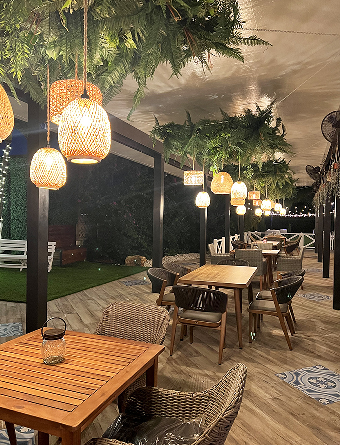 Outdoor dining elevated! Wicker chairs, wooden tables, and hanging lanterns create a garden oasis that feels miles away from city stress.