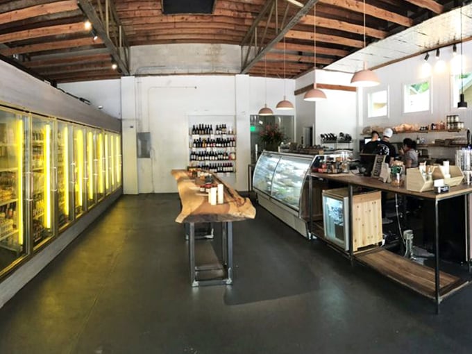 Industrial chic meets cozy comfort under exposed wooden beams, where refrigerated treasures line the wall and natural light dances across polished surfaces.