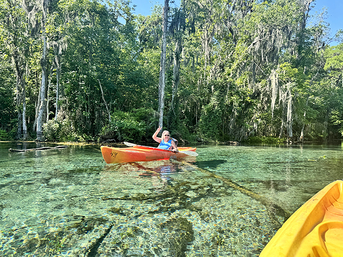 A paddler glides across water so clear it seems they're floating on air, with underwater gardens visible beneath the kayak.