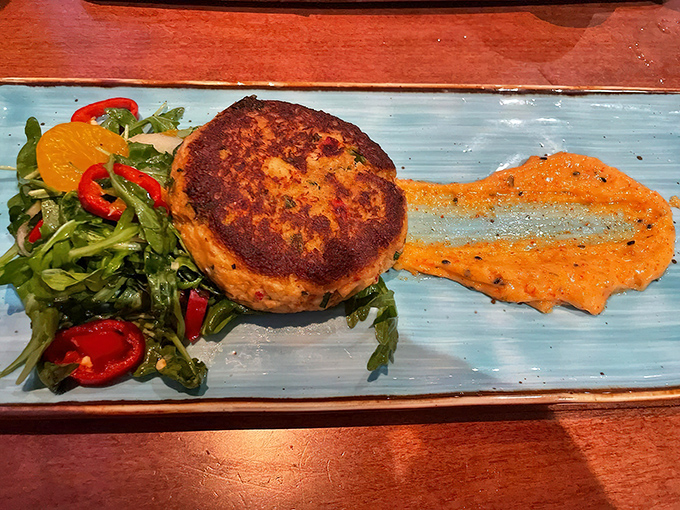 A perfectly seared seafood cake resting on a vibrant sauce &ndash; coastal cuisine that's as beautiful to look at as it is delicious to eat.