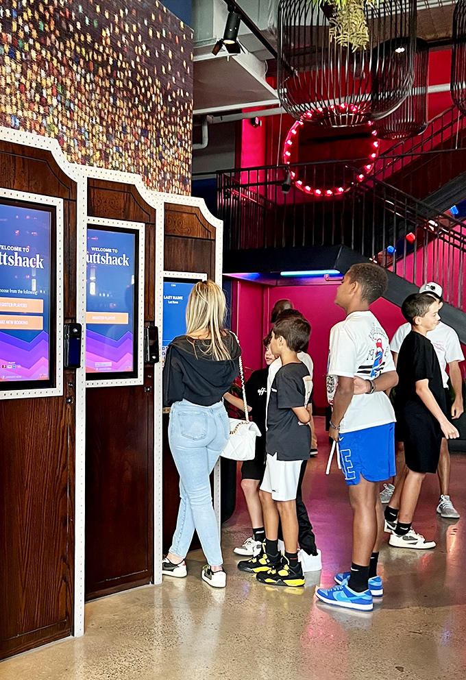 Visitors of all ages gather at the registration kiosks, eager to begin their tech-enhanced mini-golf adventure in this neon wonderland.