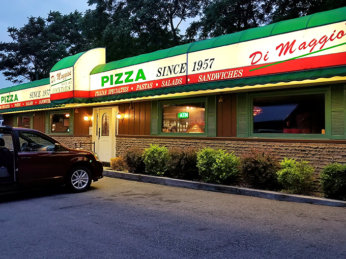 The iconic DiMaggio's storefront glows with welcome at dusk, its red, white, and green awning a beacon for pizza lovers since 1957.