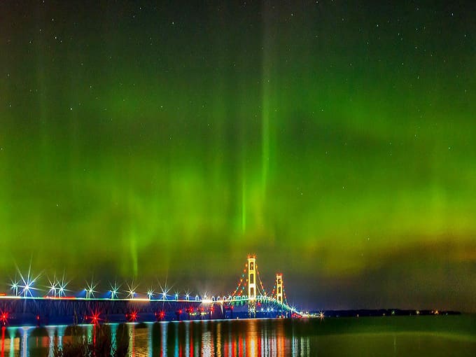 The Mackinac Bridge stands sentinel beneath a spectacular aurora display, where engineering marvel meets cosmic wonder in perfect Michigan harmony.