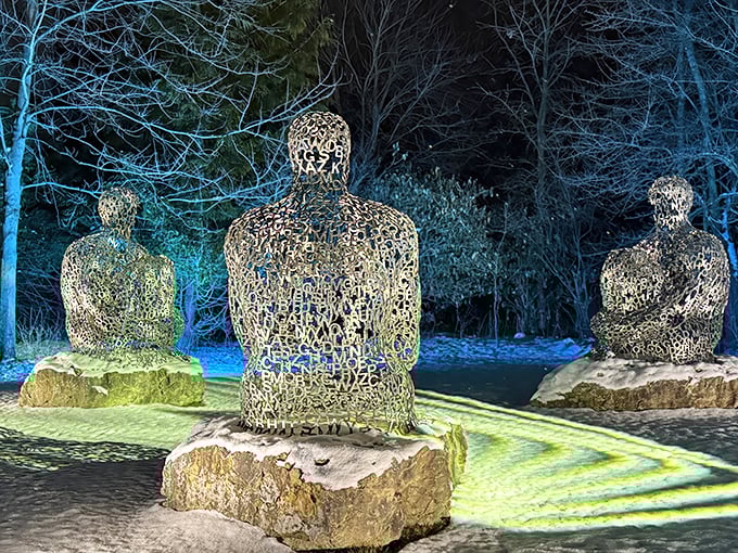 Illuminated figures stand like sentinels in the evening garden, their metal forms creating a magical, slightly otherworldly atmosphere as darkness falls.