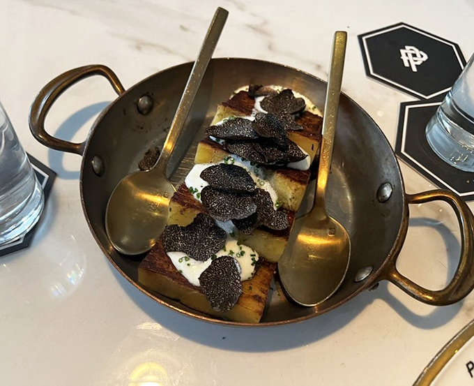 Golden potato slices crowned with black truffle &ndash; proof that sometimes the most luxurious things come in small copper pans.