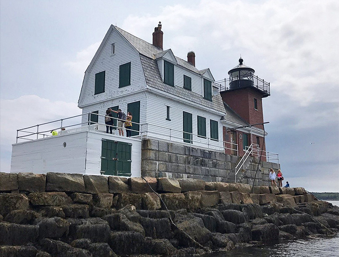 The distinctive white and red lighthouse structure appears to float on the horizon, beckoning visitors forward on their granite path journey.