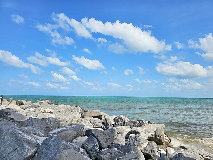 Rocky outcroppings meet turquoise waters at the lighthouse base, creating the dangerous conditions that made this beacon necessary in the first place.