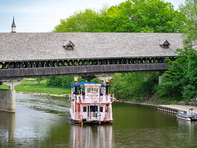 A colorful riverboat passes beneath the wooden span, creating a perfect tableau of Frankenmuth's tourist-friendly charm and old-world aesthetic.