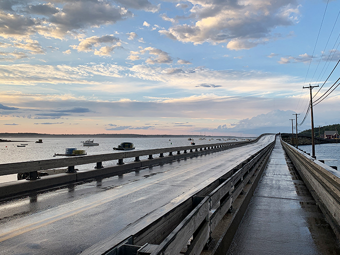 After rain showers, Bailey Island Bridge gleams in evening light, guiding travelers across waters dotted with fishing boats.