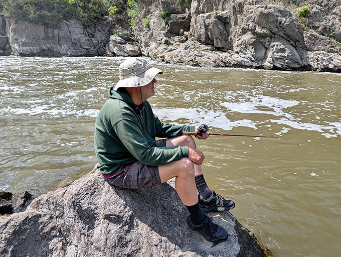 Perched on river rocks, this angler demonstrates the timeless art of fishing: equal parts sport, meditation, and excuse to sit peacefully.