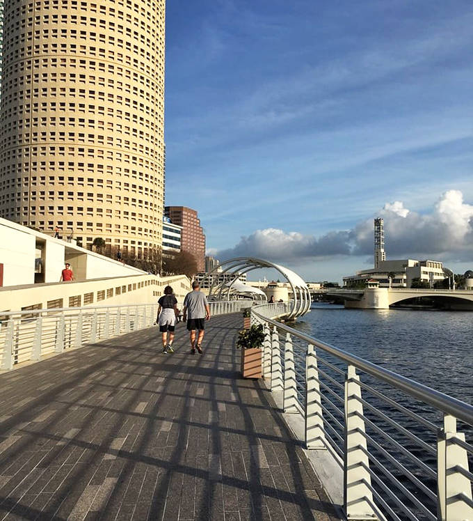 Two figures stroll into the distance, demonstrating the Riverwalk's greatest gift: human-scale access to monumental urban beauty.