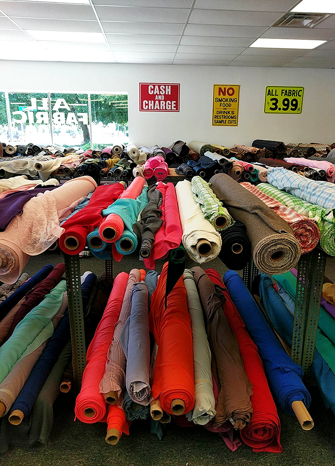 A textile explosion of color and texture greets shoppers, with bolts stacked so high they create fabric skyscrapers reaching toward the fluorescent heavens.