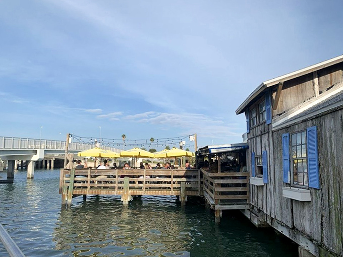 The waterfront dining deck hovers just above the gentle waves, yellow umbrellas creating pools of shade perfect for lingering over lunch.