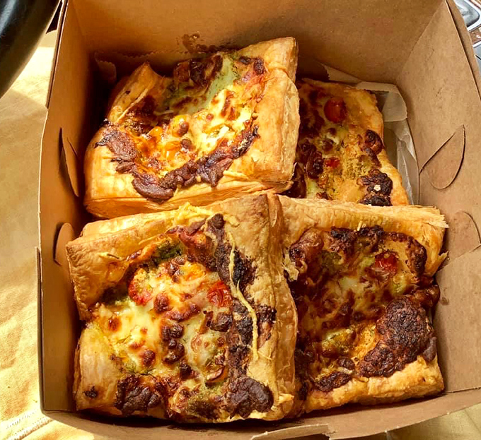 Savory pastry squares nestled in their box like edible presents, with cheese melted to golden perfection on top.