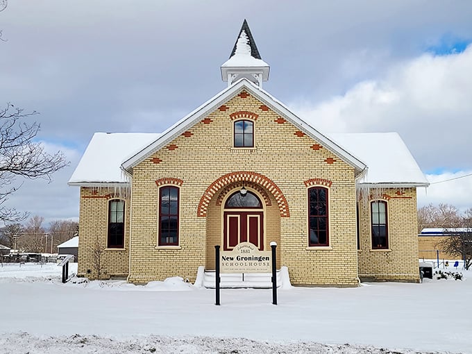 The New Groningen Schoolhouse stands proudly against winter's white canvas, its yellow brick and bell tower preserving educational heritage for future generations.