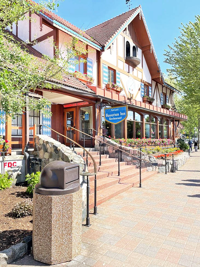 Sunshine bathes the Bavarian-style architecture, highlighting the flower boxes and distinctive blue-and-white Bavarian pattern that adorns the windows.