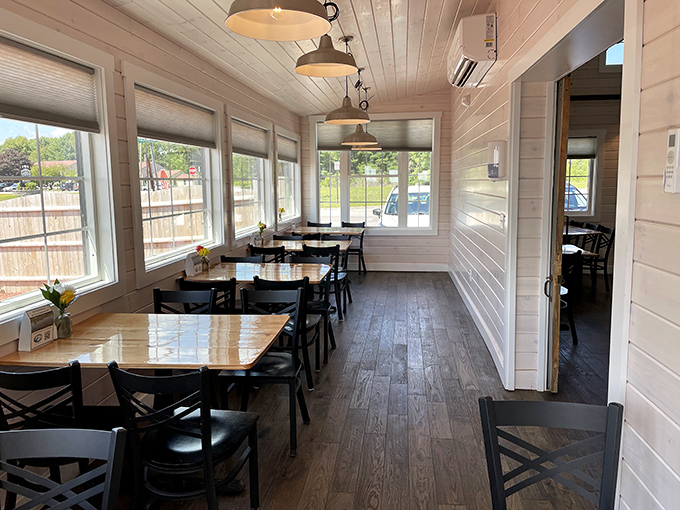 Natural light floods the dining area through generous windows, the white wood paneling creating a bright, airy space that welcomes guests like old friends.