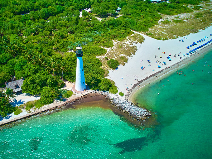 From above, the lighthouse appears as nature intended &ndash; a solitary white sentinel standing guard where emerald forest meets turquoise sea.