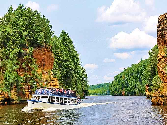 Tourists marvel at towering sandstone cliffs from a tour boat in the Wisconsin Dells, where the river has carved natural wonders.