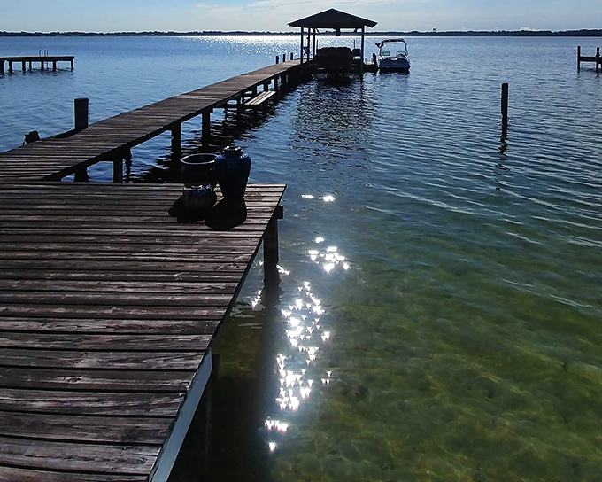 Sunlight creates diamonds across clear waters, while a wooden dock invites you to leave your worries on the shore.