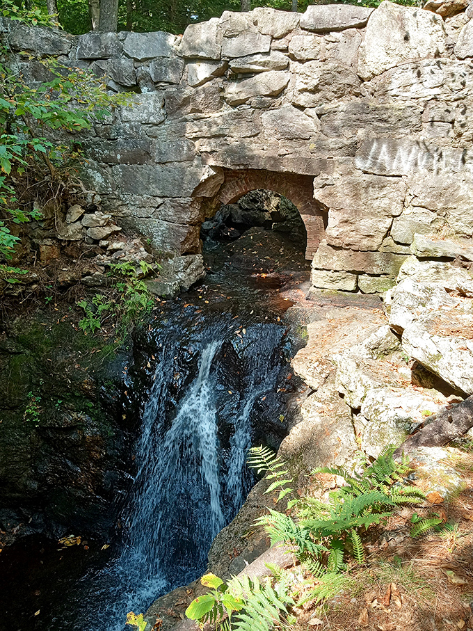 The historic stone arch at Snow Falls frames the cascading water perfectly, creating nature's own picture window into wilderness beauty.