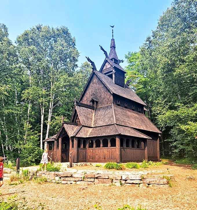 Summer sunlight bathes the Stavkirke's weathered timbers, its distinctive silhouette rising from the forest floor like a medieval vision in Wisconsin's northwoods.