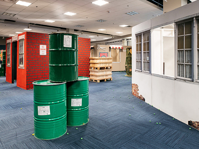 Green barrels and wooden crates transform this indoor battlefield into an urban tactical playground where strategy trumps strength.