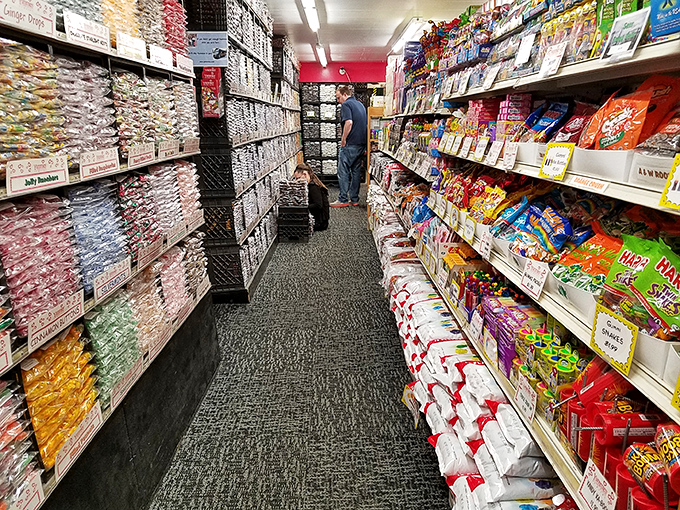 Narrow aisles create a candy labyrinth where treasure hunters navigate between towering walls of packaged treats, each turn revealing new sugary discoveries.