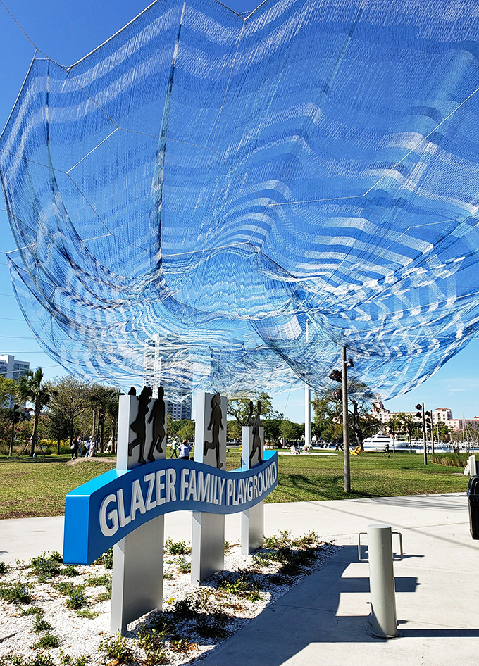 The iconic entrance to Glazer Family Playground, where silhouetted figures dance across pillars beneath a billowing blue net sculpture.