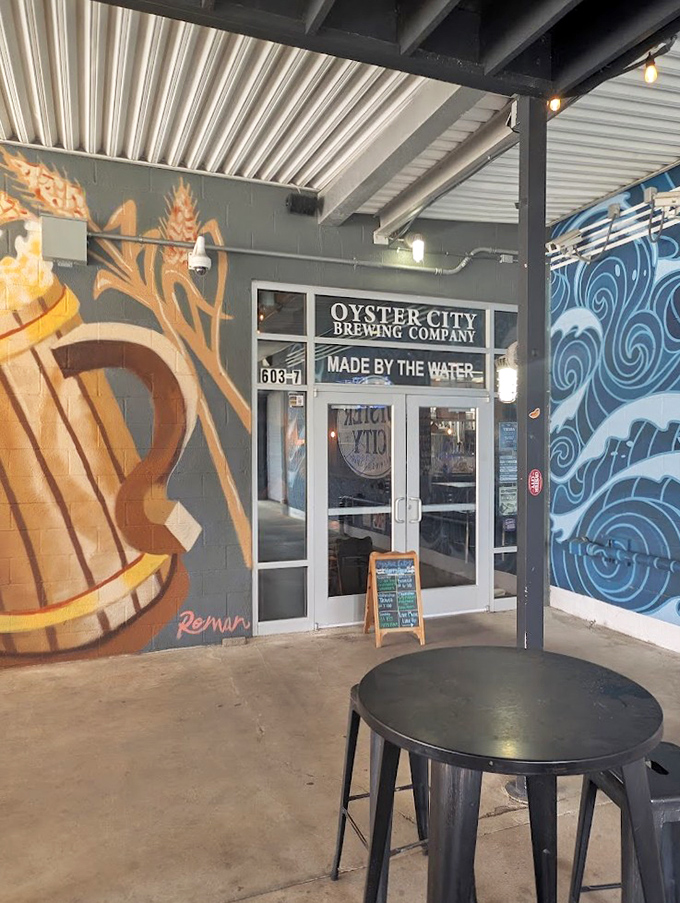 Vibrant murals and coastal-inspired art surround the entrance to Oyster City Brewing Company, showcasing their "Made By The Water" philosophy.