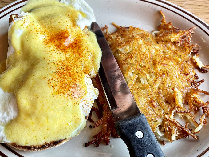 A classic breakfast plate featuring eggs smothered in creamy hollandaise sauce, served with crispy golden hash browns on the side.