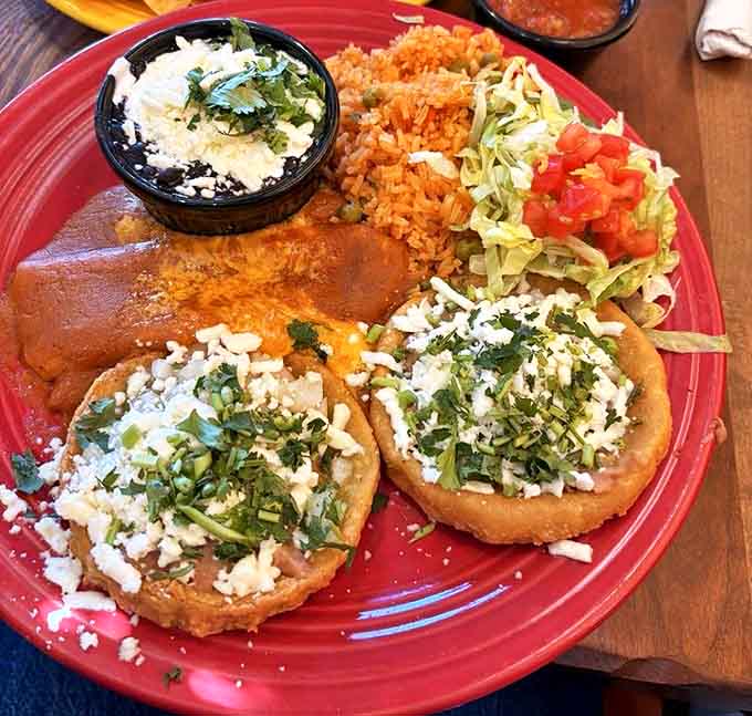 Sopes crowned with fresh cheese and herbs share the spotlight with enchiladas draped in rich sauce – a fiesta of textures and flavors on one vibrant plate.