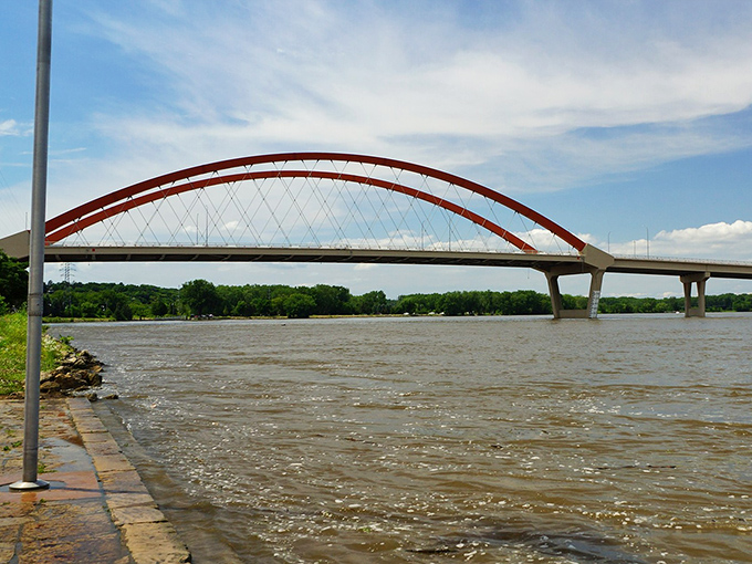 Hastings Bridge arches dramatically over the Mississippi, its distinctive red span creating a perfect frame for river traffic below.