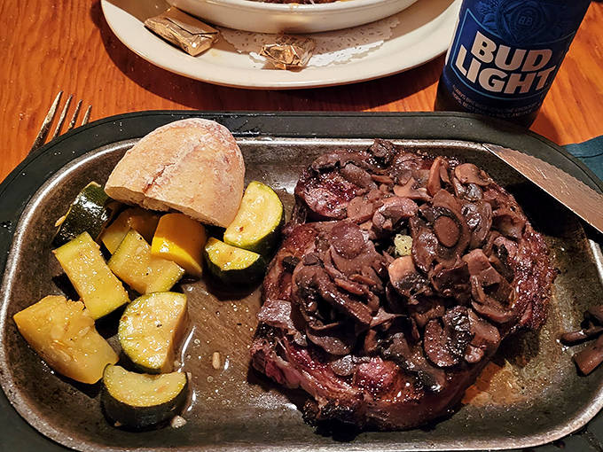 A perfectly seared ribeye topped with saut&eacute;ed mushrooms sits alongside seasonal vegetables, a carnivore's dream realized on a sizzling platter.