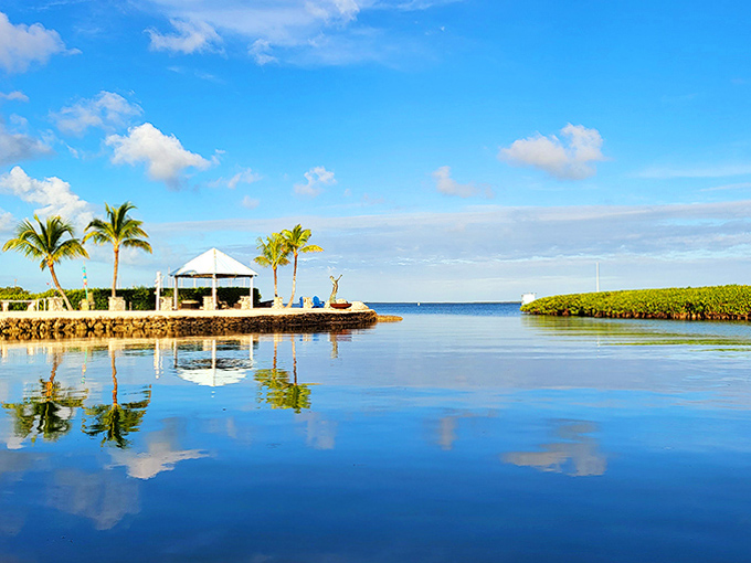 A white gazebo stands sentinel on the shoreline, where palm trees sway and reflections dance across waters so still they mirror the sky.