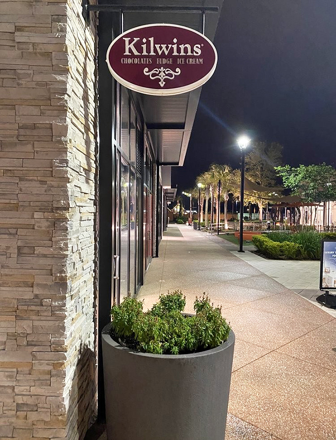 Kilwins' storefront glows invitingly at night, promising sweet adventures for anyone drawn to its famous chocolates and homemade treats.