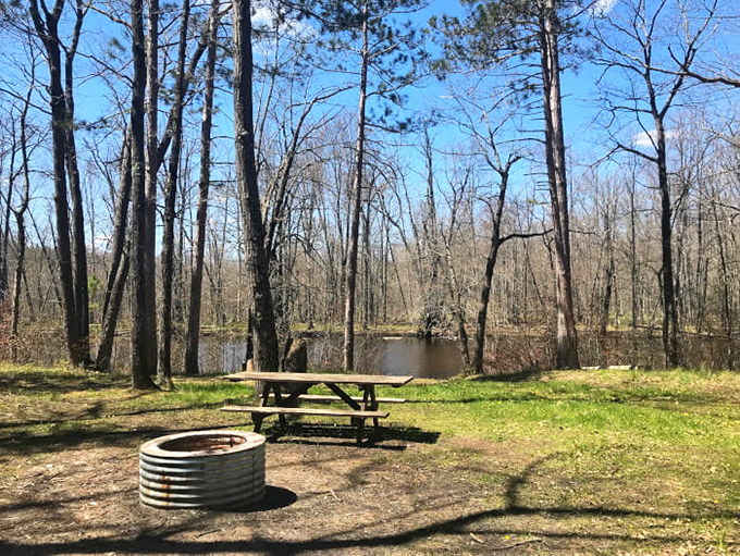 A simple picnic table and fire ring invite contemplation beside still waters, where lumberjacks once drove massive log rafts downstream.