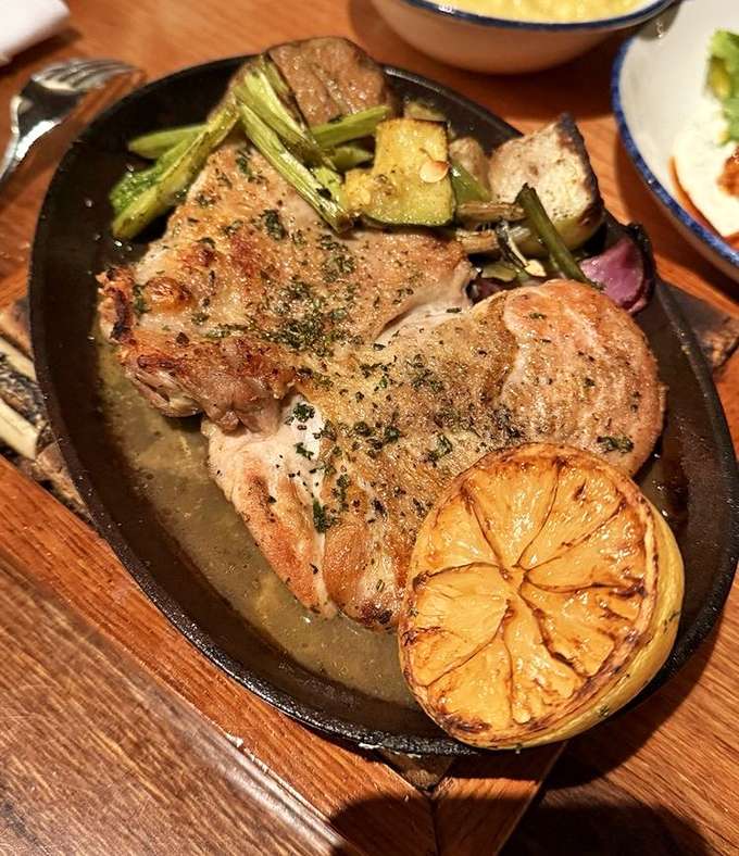 Perfectly cooked chicken rests beside seasonal vegetables, with a charred lemon adding bright acidity to this comforting yet refined plate.