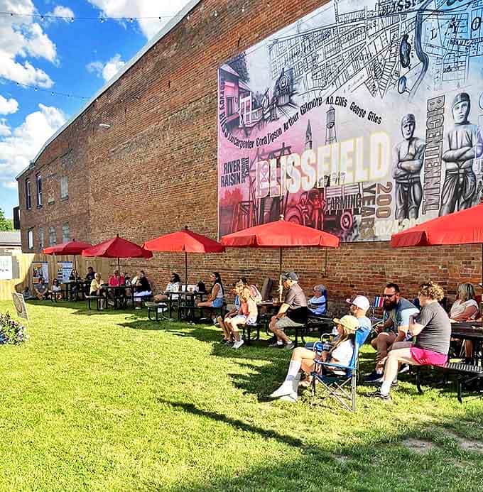 Locals gather under red umbrellas beside a vibrant mural celebrating Blissfield's heritage &ndash; community happens naturally in these outdoor spaces.
