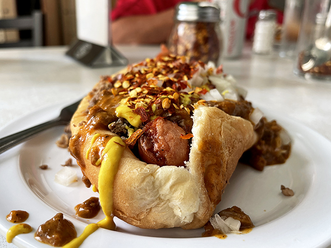Behold the masterpiece: a perfectly dressed coney dog with chili, mustard, and onions creating layers of pure deliciousness.