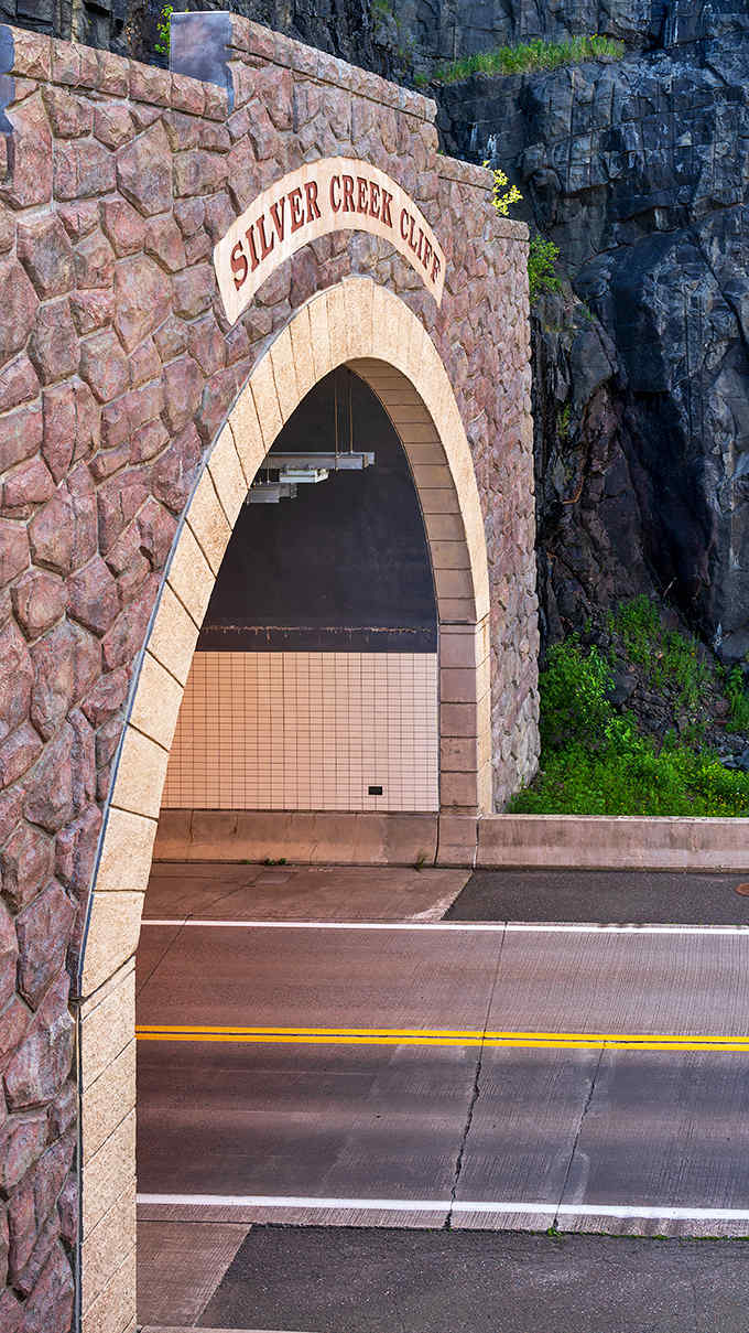 The tunnel's elegant stonework frames the entrance like a picture window, inviting travelers to pass through the mountain rather than risk the treacherous edge.