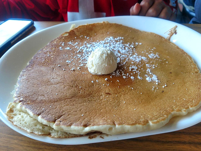 A pancake so fluffy it practically floats above the plate, crowned with a melting butter pat and dusted with powdered sugar.