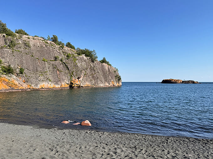 The beach curves along the shoreline like nature's own amphitheater, with Lake Superior providing the entertainment and the dark sand setting the stage.