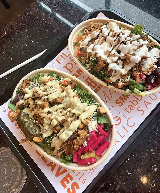Two bowls of chicken shawarma glory, dressed to impress with colorful toppings and drizzled with creamy sauces.