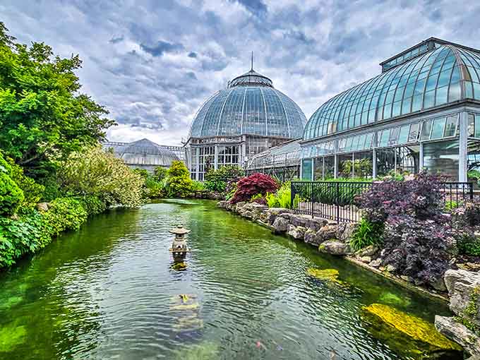 The serene Japanese garden pond outside reflects the conservatory dome, creating a perfect harmony between architecture and nature.
