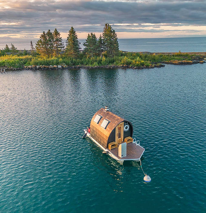 The floating sauna appears tiny against Minnesota's vast wilderness, a wooden comma in nature's endless paragraph.
