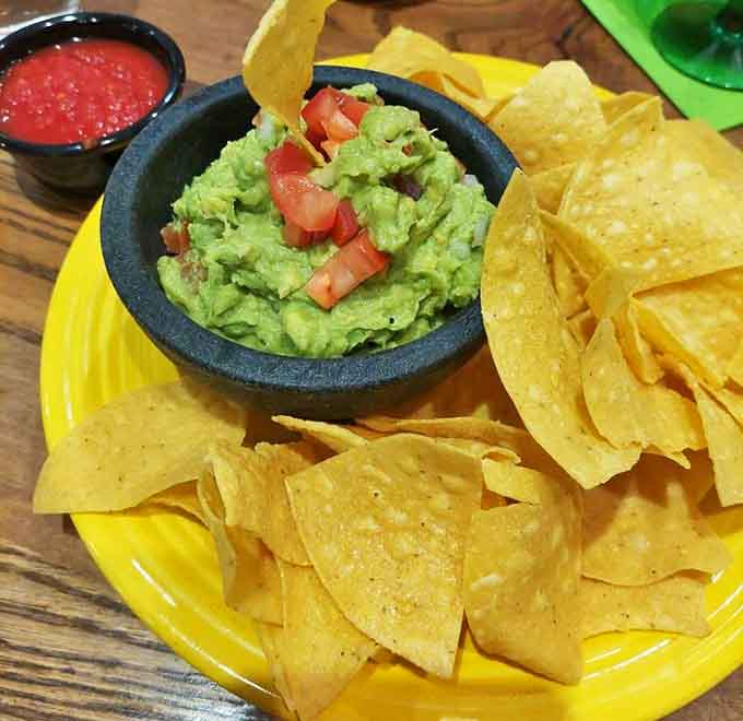 Fresh guacamole nestled in a sunny yellow plate with crisp tortilla chips standing at attention – simple perfection that never goes out of style.