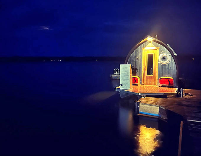 Night falls on Lake Superior as the sauna glows like a lantern, its warm light a beacon of coziness in the darkness.