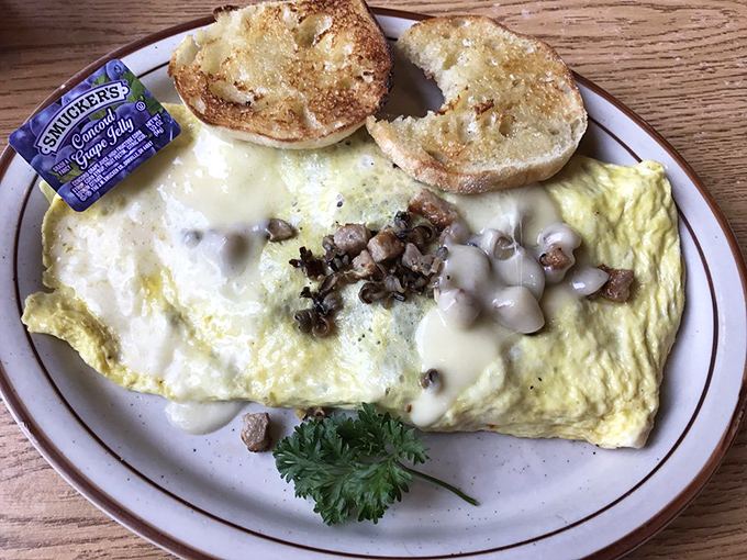 A fluffy omelet filled with diced meat and topped with rich gravy, served alongside buttered toast for a comforting diner-style breakfast.