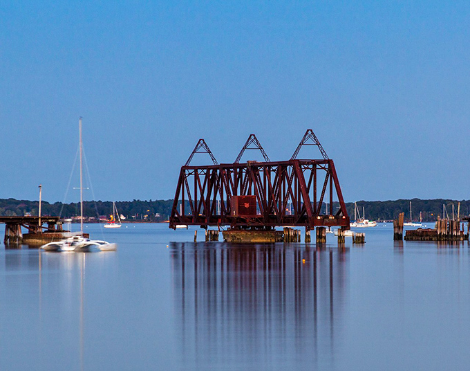 The abandoned rail bridge creates perfect reflections on calm days, doubling the visual impact of this magnificent industrial dinosaur.
